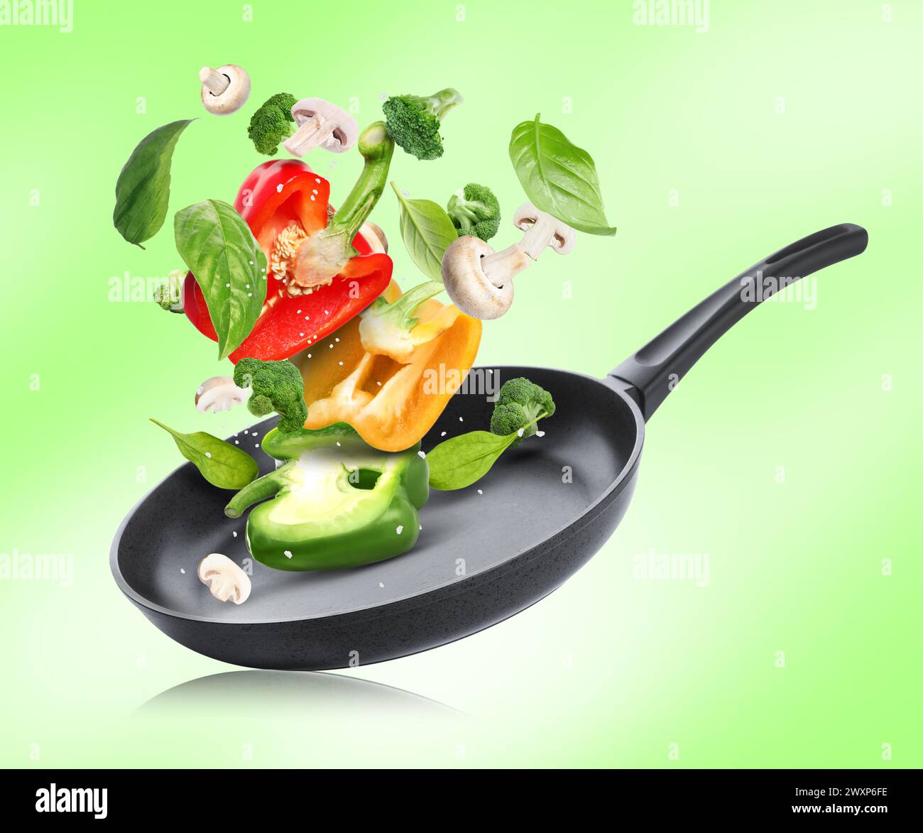 Frying pan with fresh ingredients in air on green background Stock ...
