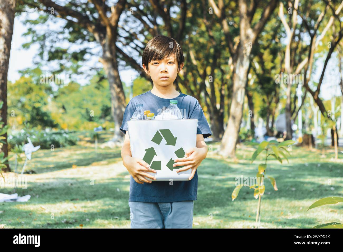 Cheerful young asian boy holding recycle symbol bin on daylight natural ...
