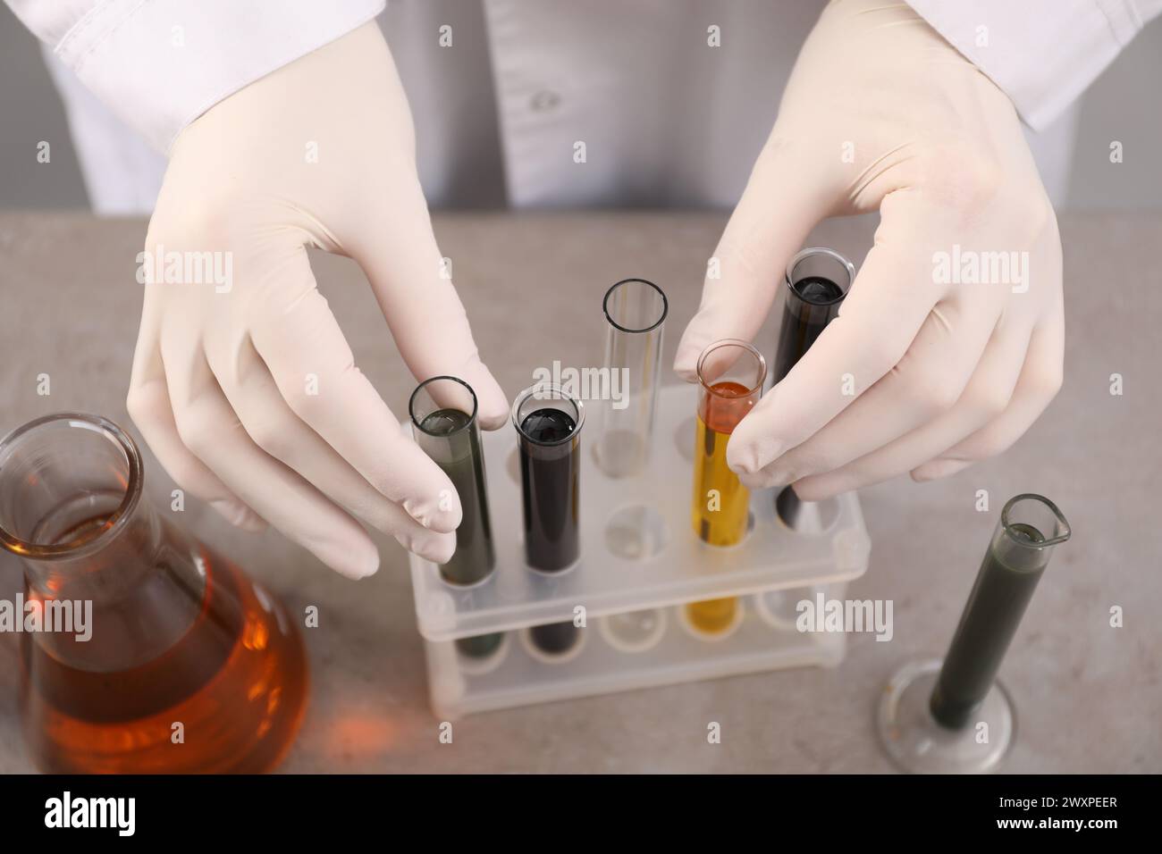 Woman taking test tubes with different types of crude oil from rack at ...