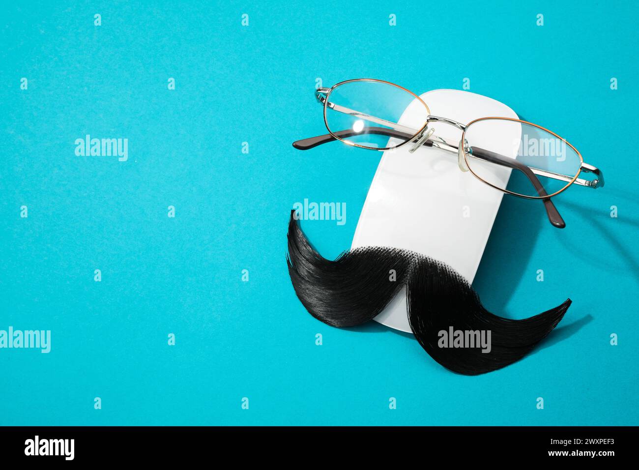 Artificial moustache, computer mouse and glasses on light blue ...