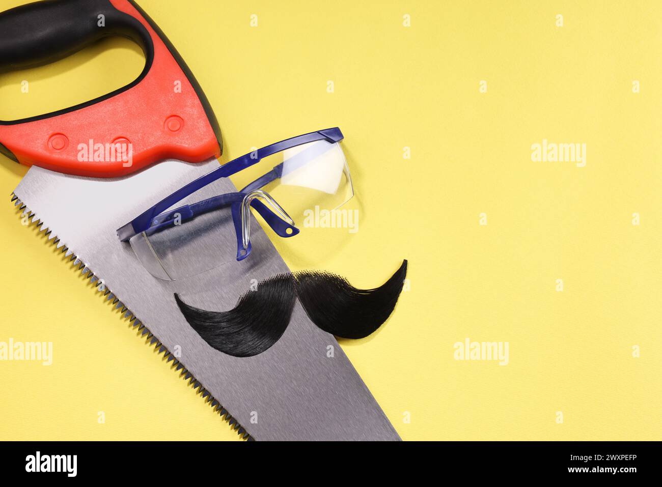 Man's face made of artificial mustache, safety glasses and hand saw on ...