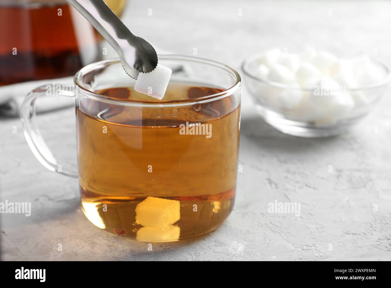 Adding sugar cube into cup of tea at grey textured table, closeup Stock ...