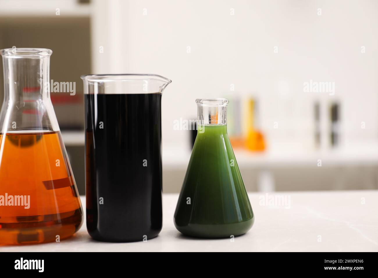 Flasks and beaker with different types of crude oil on light marble ...