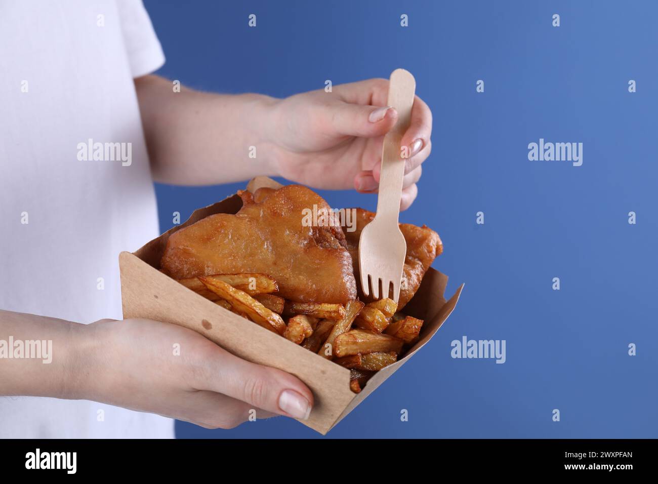 Woman eating fish and chips on blue background, closeup. Space for text ...