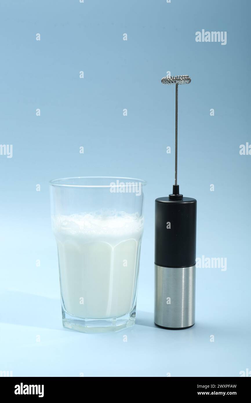 Mini mixer (milk frother) and whipped milk in glass on light blue ...