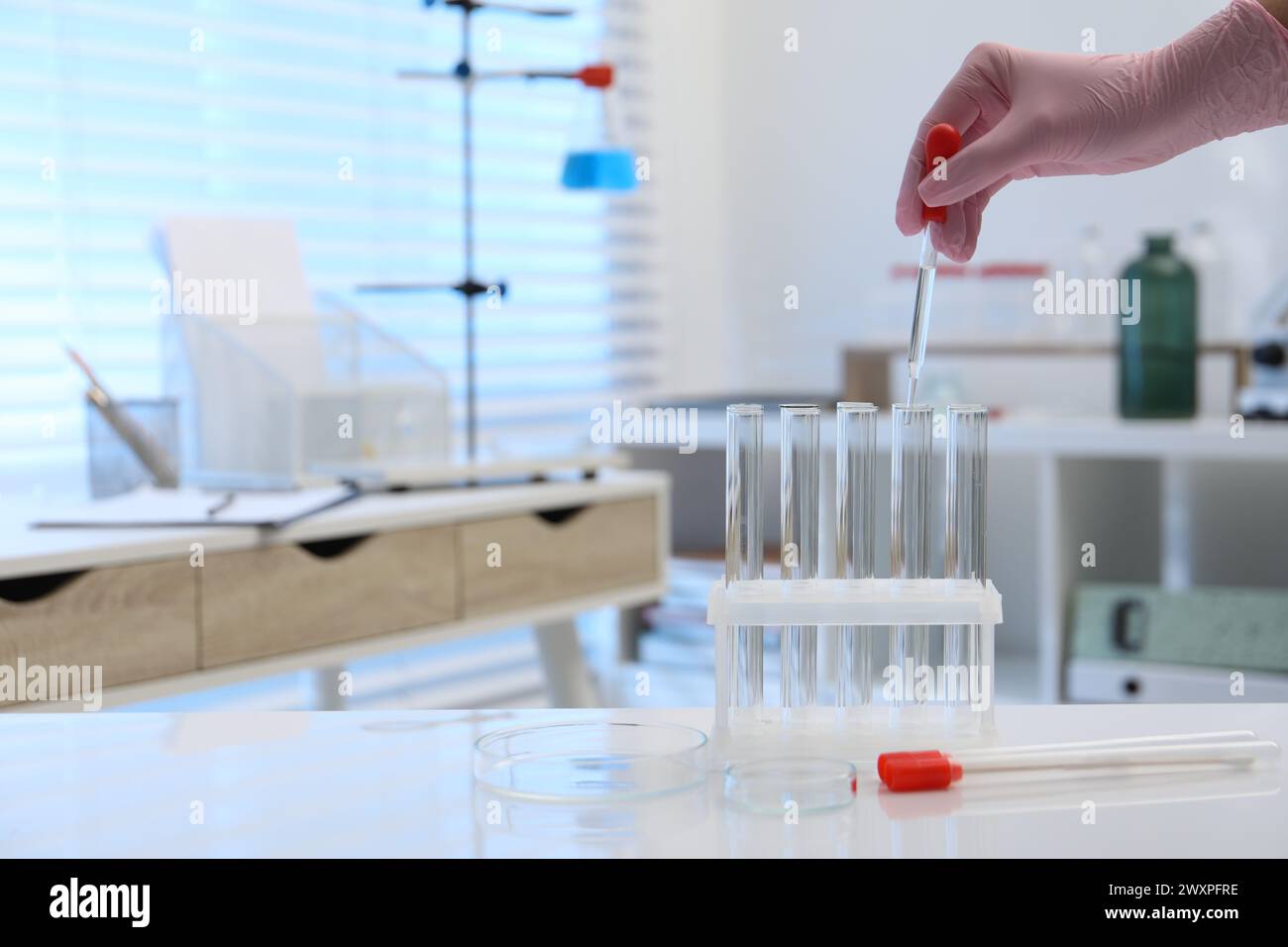 Laboratory analysis. Woman dripping liquid into test tubes at white ...