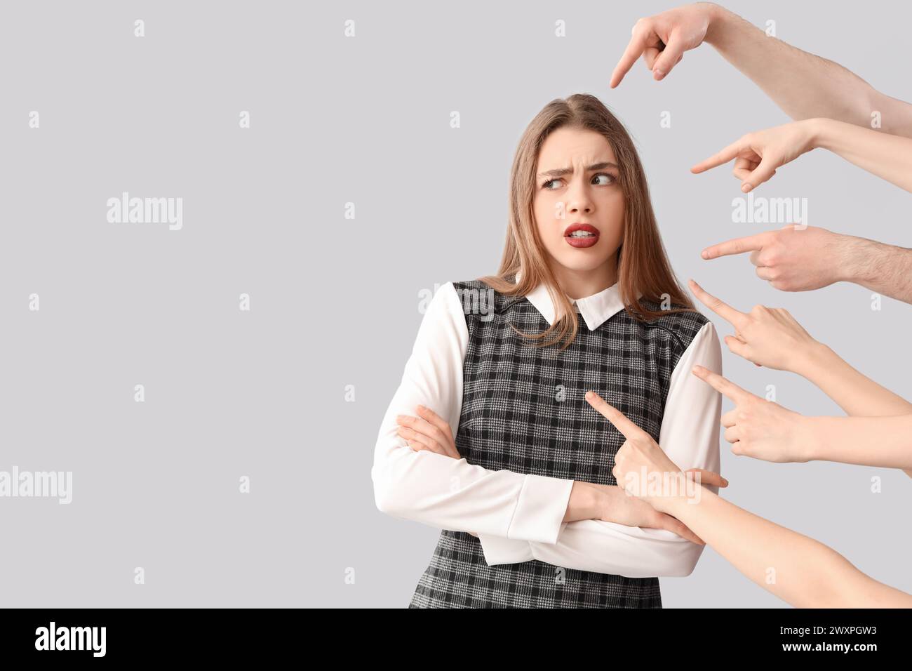 People pointing at displeased young businesswoman on light background ...