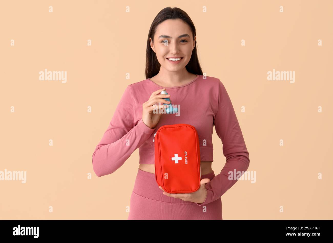 Sporty young woman with inhaler and first aid kit on beige background ...