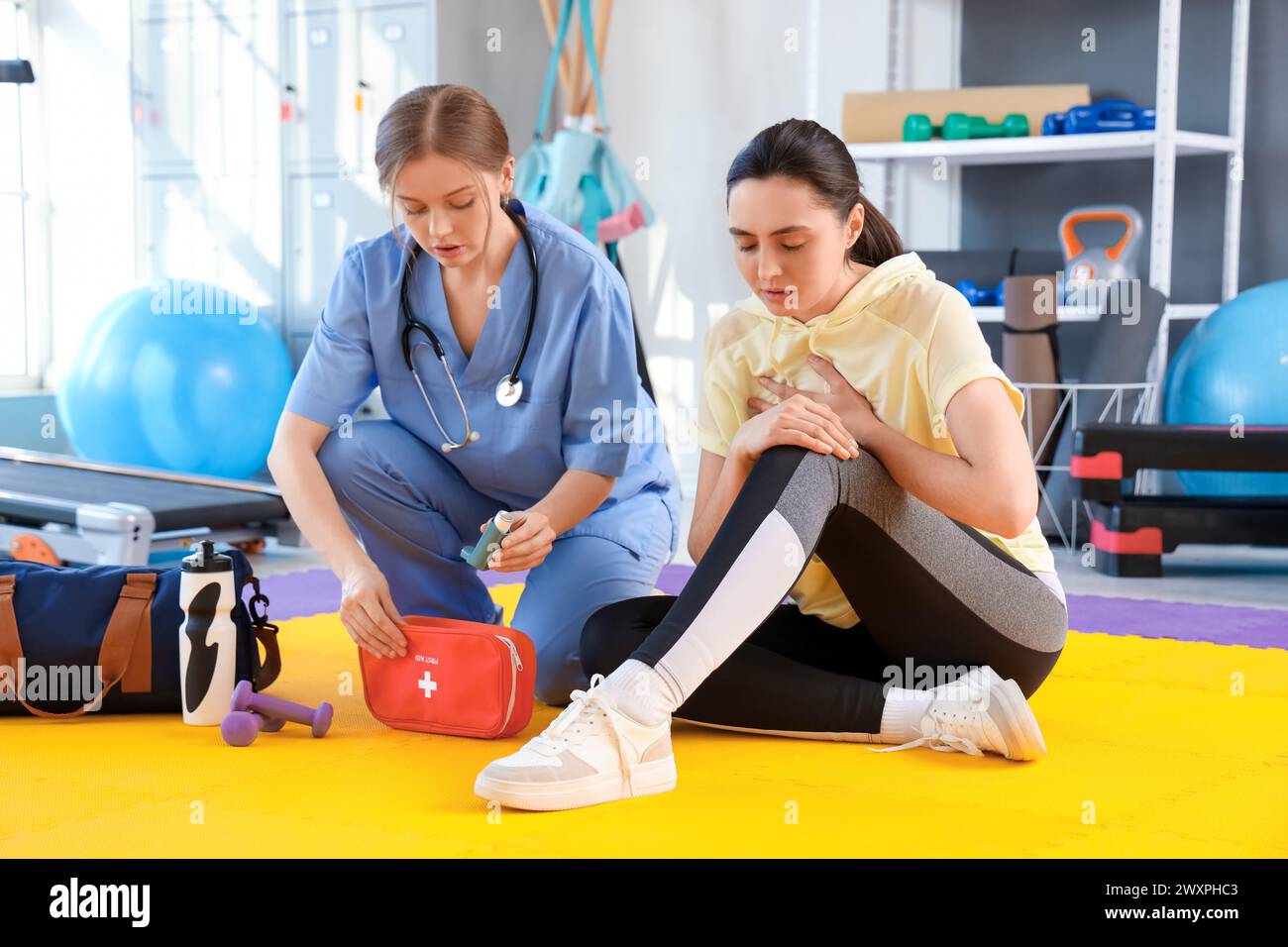 Female doctor with inhaler giving young woman first aid in gym Stock ...