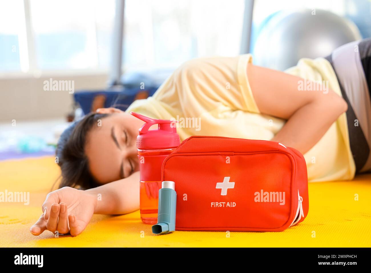 Inhaler with first aid kit, water bottle and unconscious woman in gym ...