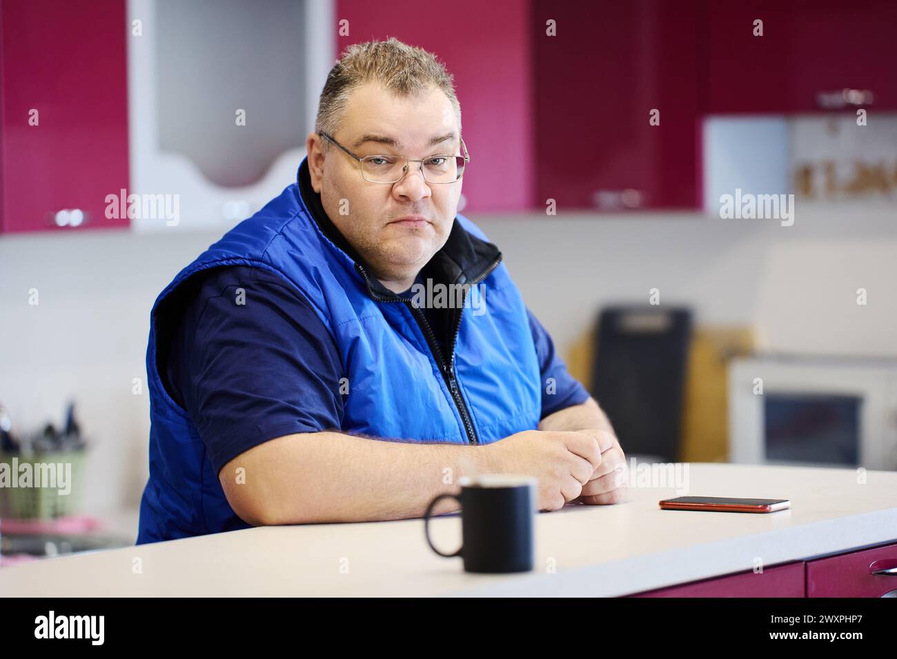 Sad large build man sits in front of kitchen island Stock Photo - Alamy