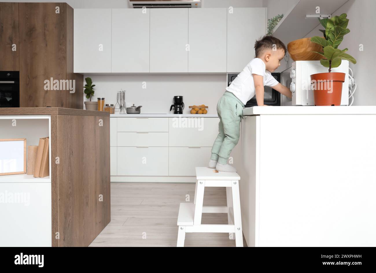 Little boy on step stool opening microwave oven in kitchen. Child at ...