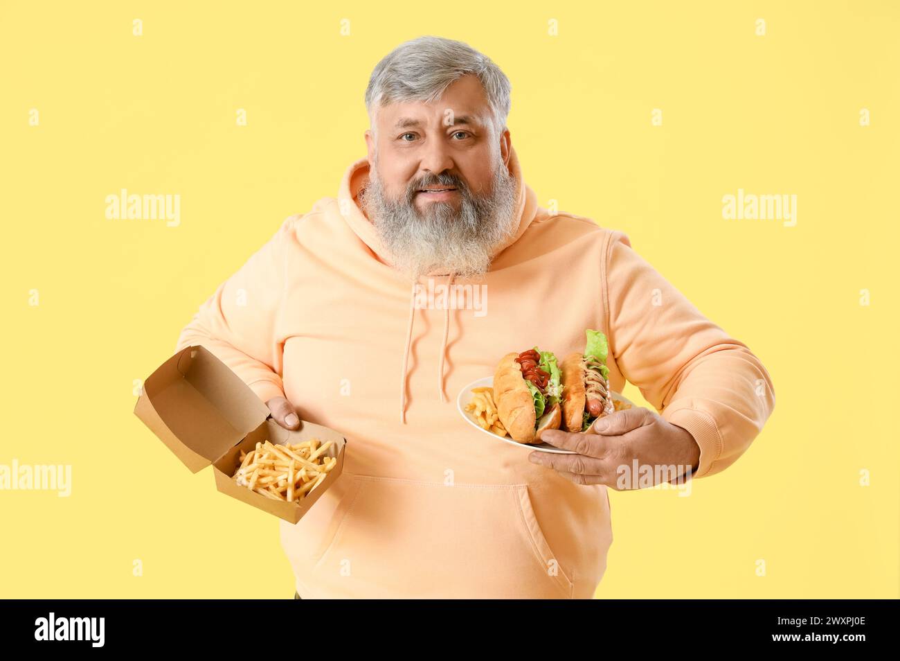Overweight mature man with hot dogs and french fries on yellow ...