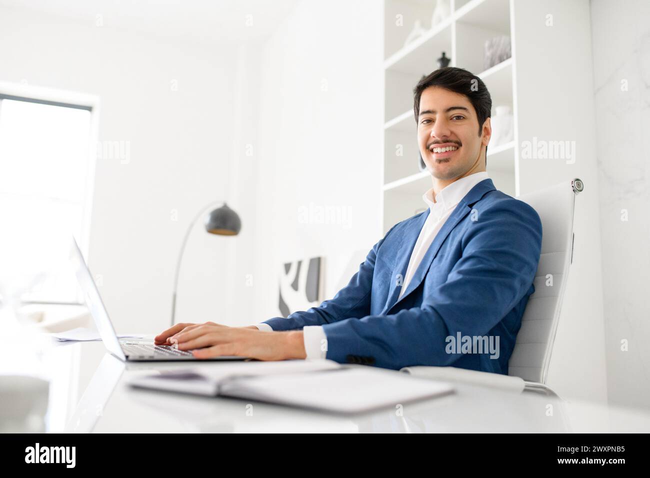 An affable Hispanic businessman smiles, looks at the camera while using ...