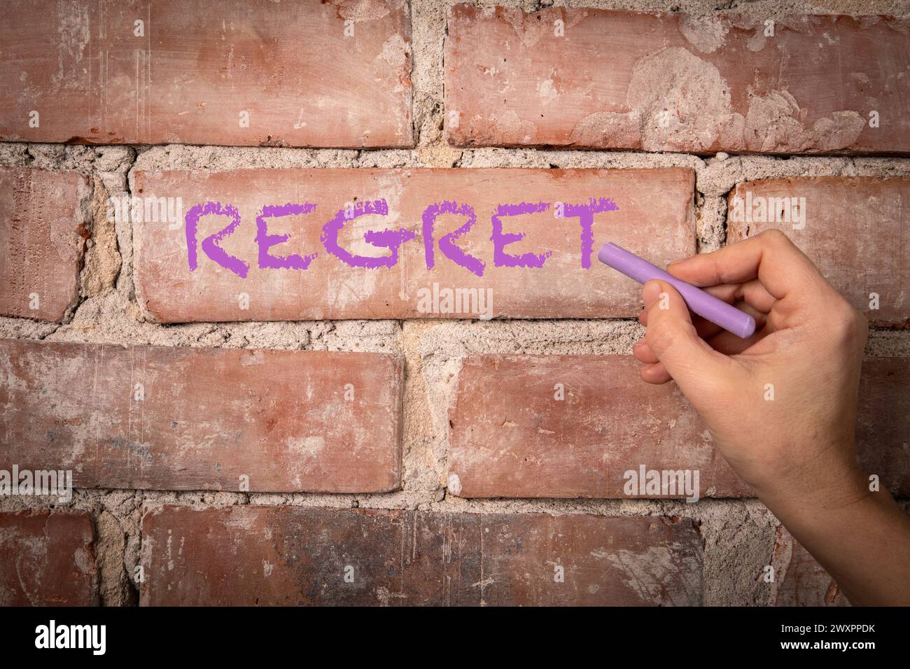 REGRET. Text written with purple chalk on a red brick background Stock ...