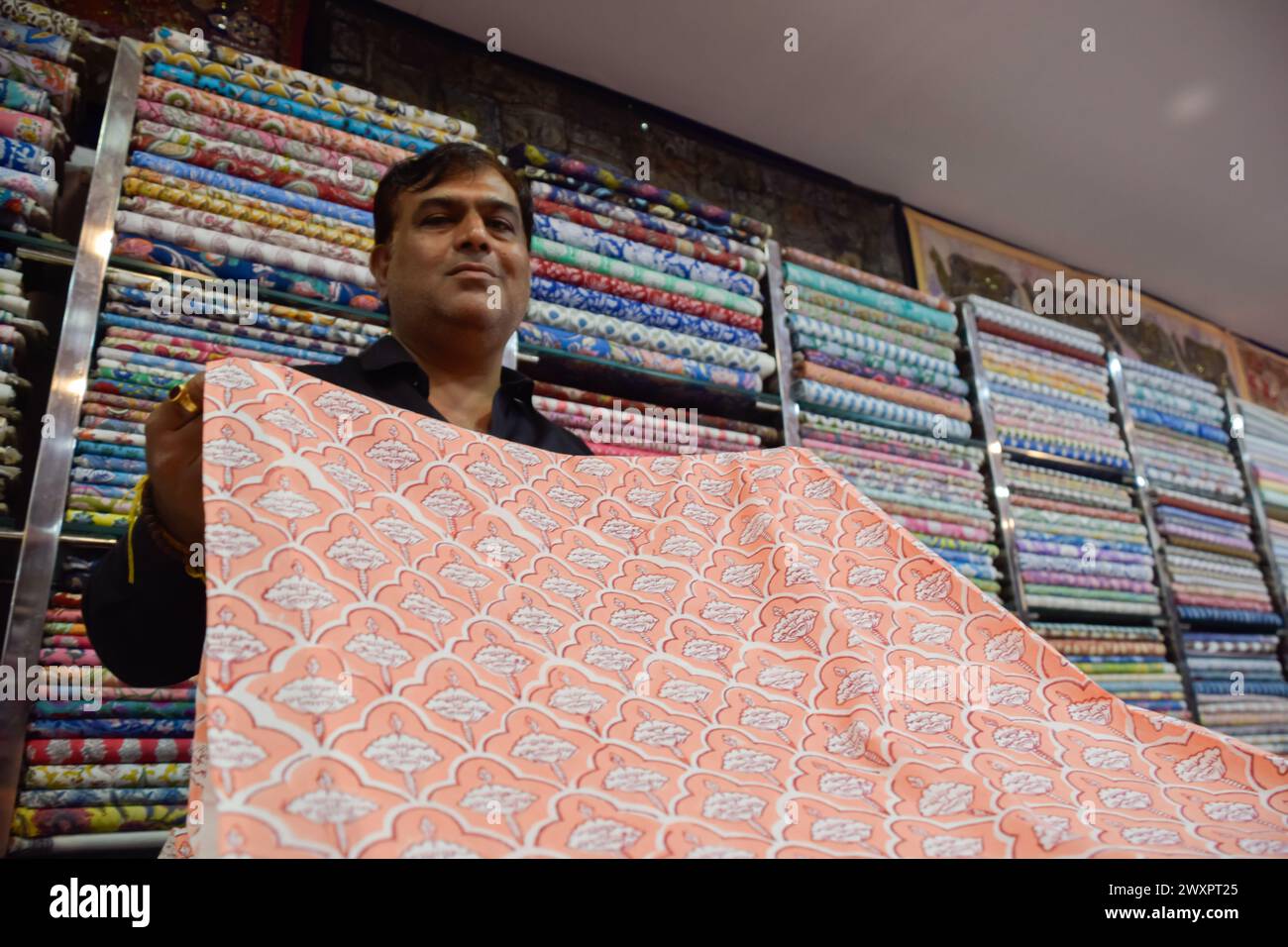 Indian seller showing textiles with variety of colors in shop of a ...