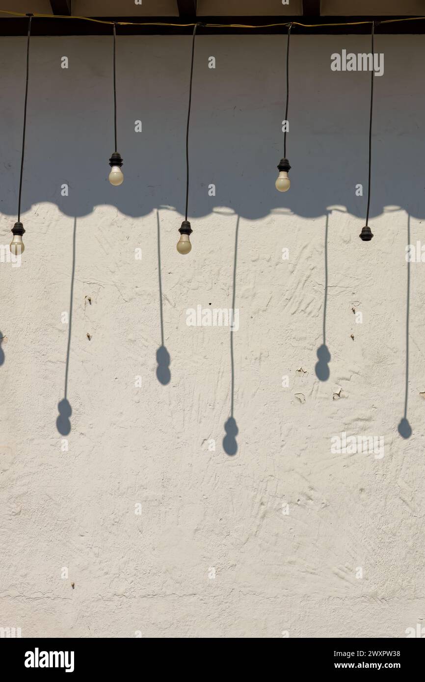 Some hanging bulbs cast their shadow on a white wall in the afternoon ...