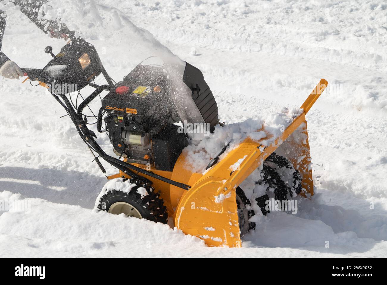 Worker with motor snow blower clearing snow from road after winter storm, assisted by snow ...