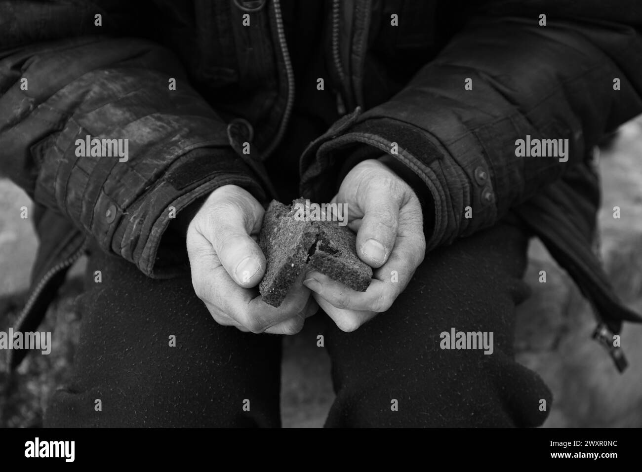 Poor homeless man holding piece of bread outdoors, closeup. Black and ...