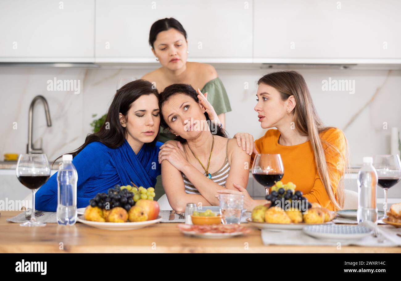 Sad Spanish woman sits silently in kitchen, female friends sympathize and comfort woman Stock ...
