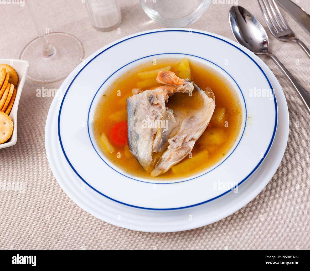 Fish broth with salmon head and vegetables served with salty crackers ...