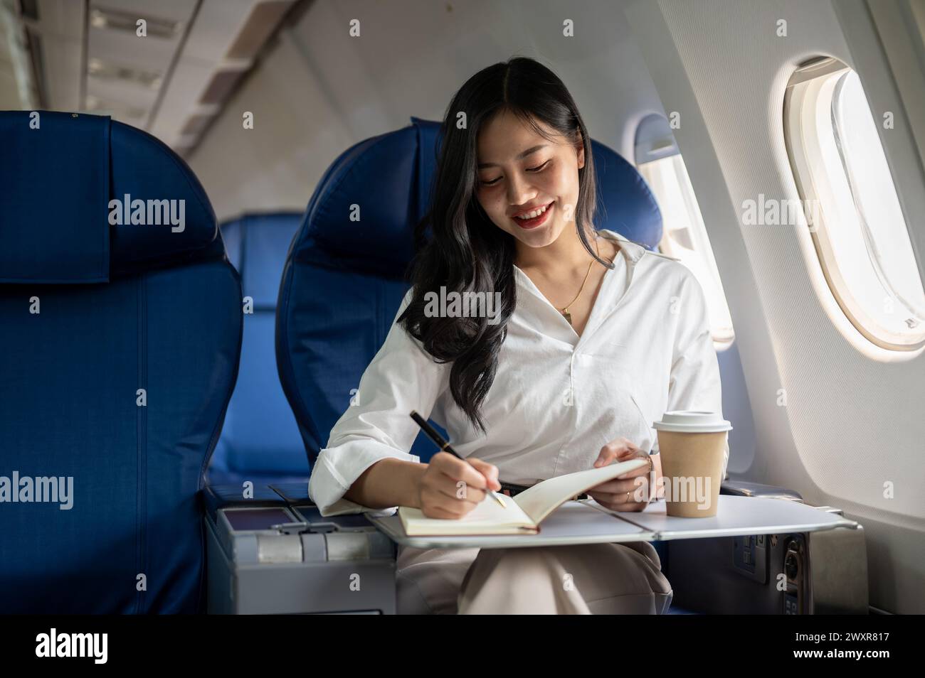 An attractive Asian businesswoman is taking notes in her notebook while ...
