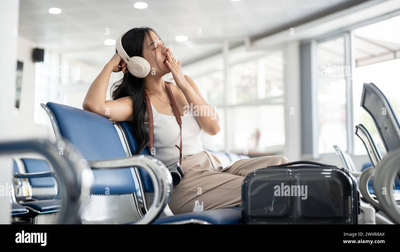 A bored and tired Asian female passenger is yawning and feeling sleepy while waiting for her ...