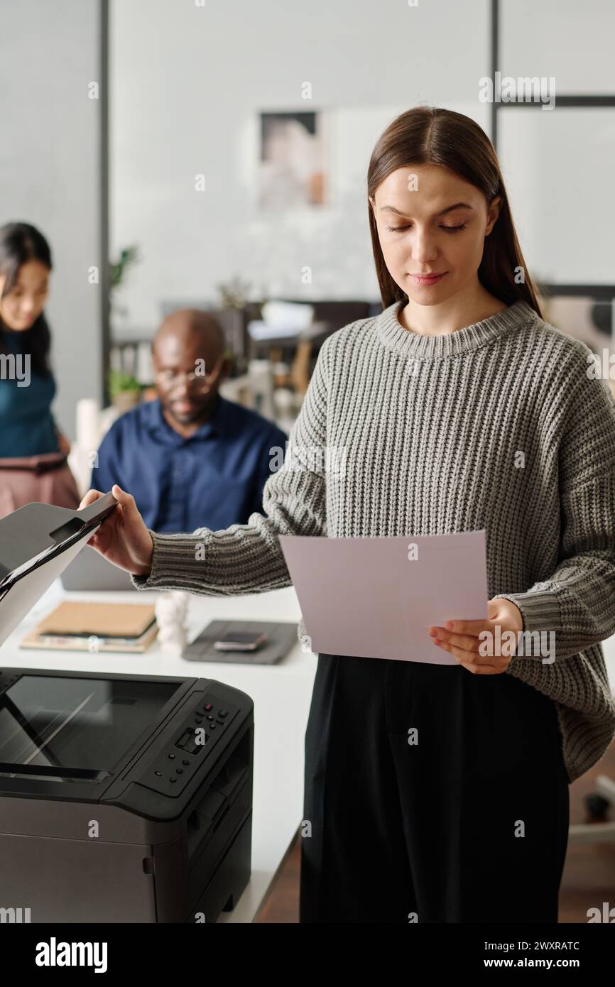 Vertical medium long shot of young Caucasian woman checking document ...