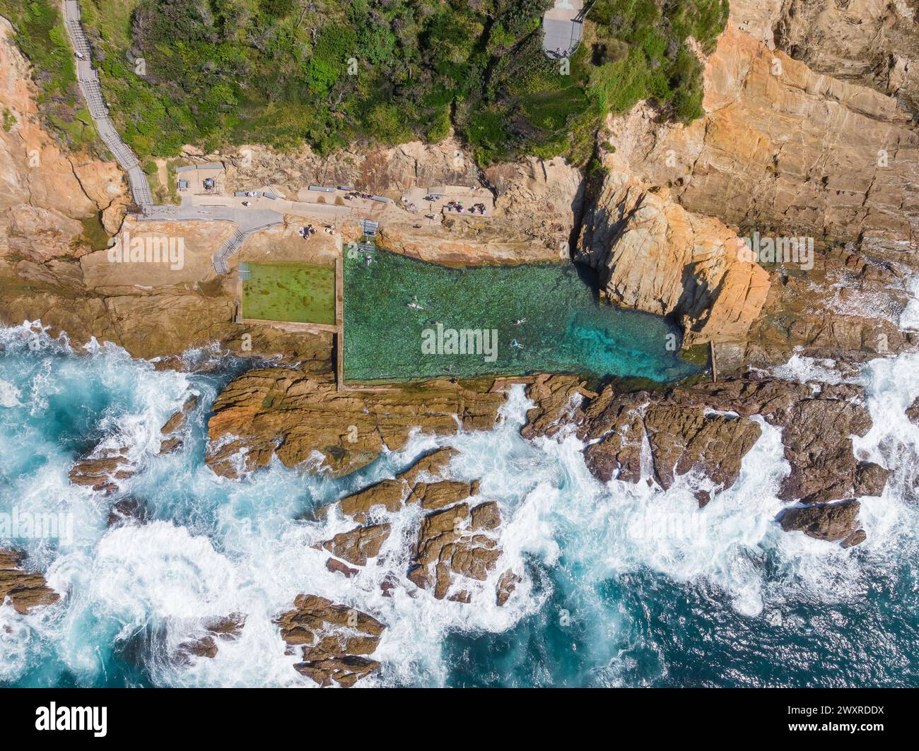 Aerial view of an waves breaking around a coastal rock pool at the base ...