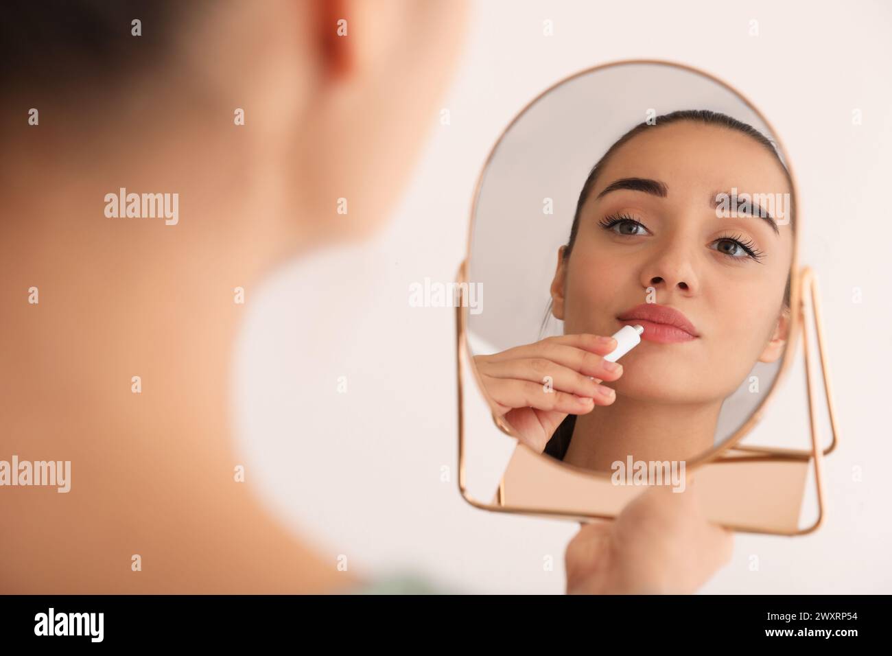 Woman with herpes applying cream on lips in front of mirror against ...