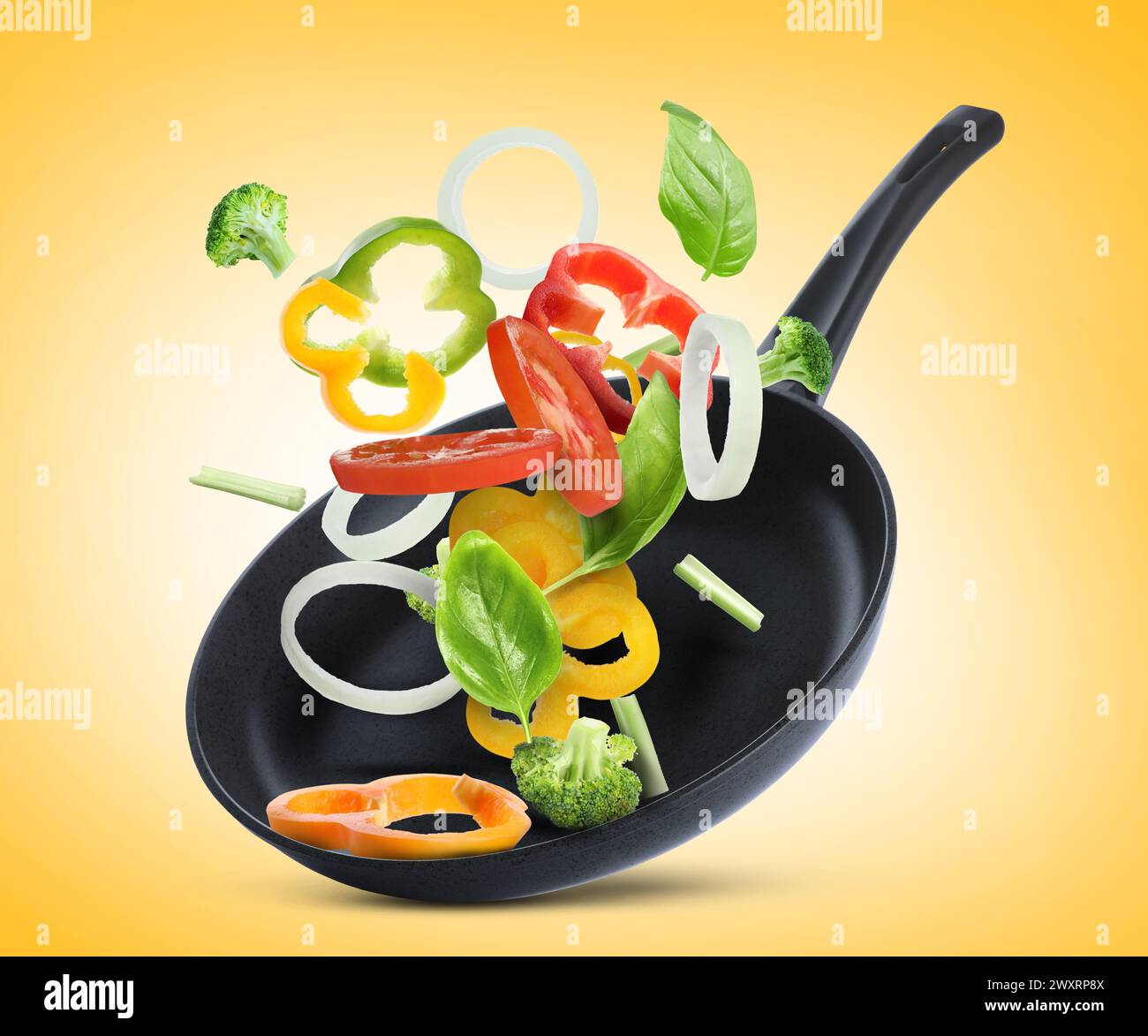 Frying pan with fresh ingredients in air on golden background Stock ...