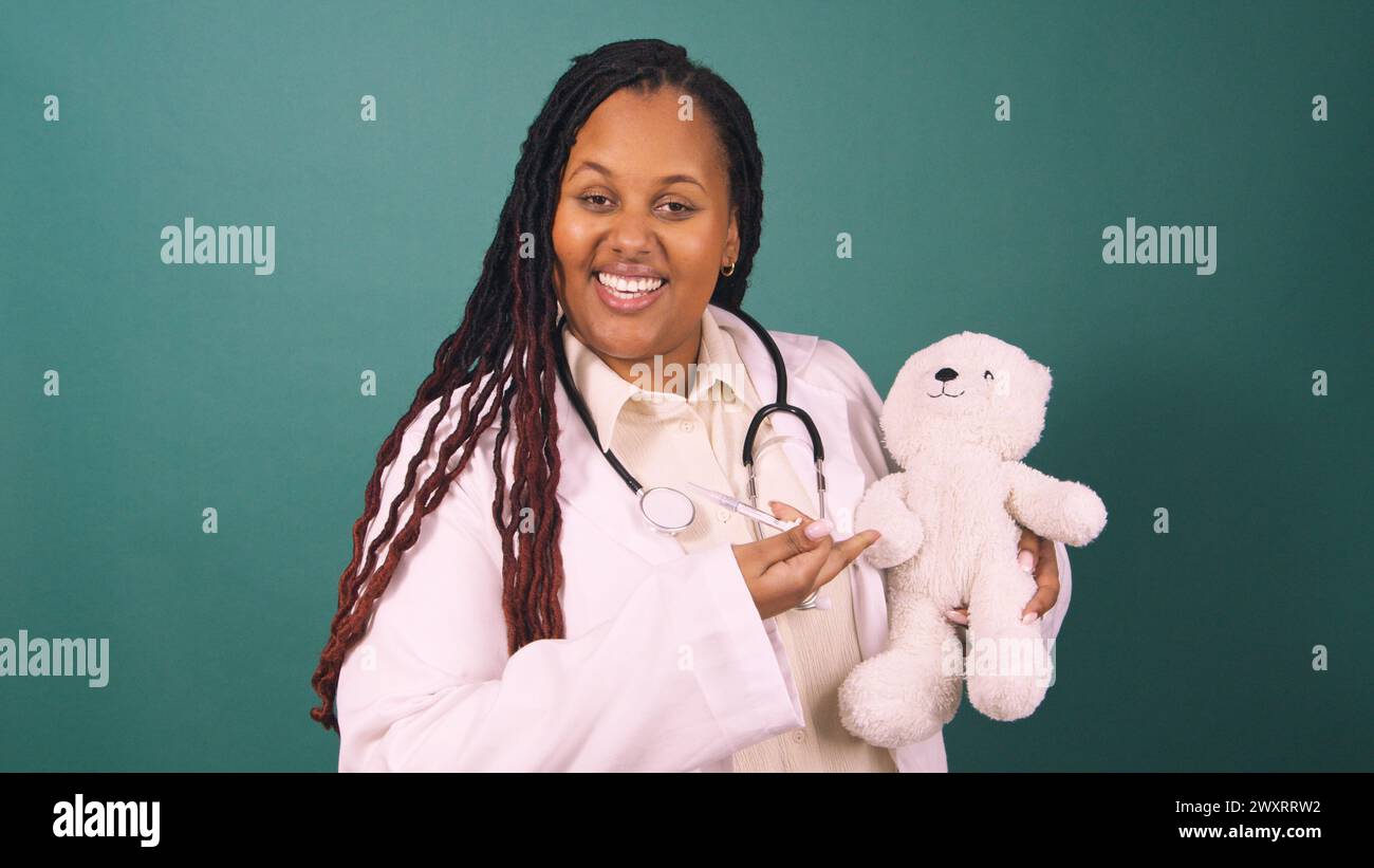 Young Black female doctor demonstrates an injection, using teddy bear ...