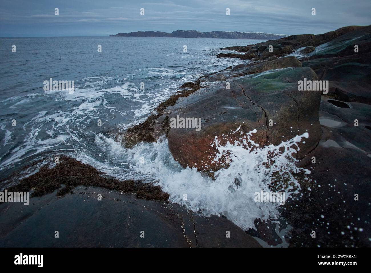 Sea spray rises as waves meet a rugged coastline, all under a brooding ...