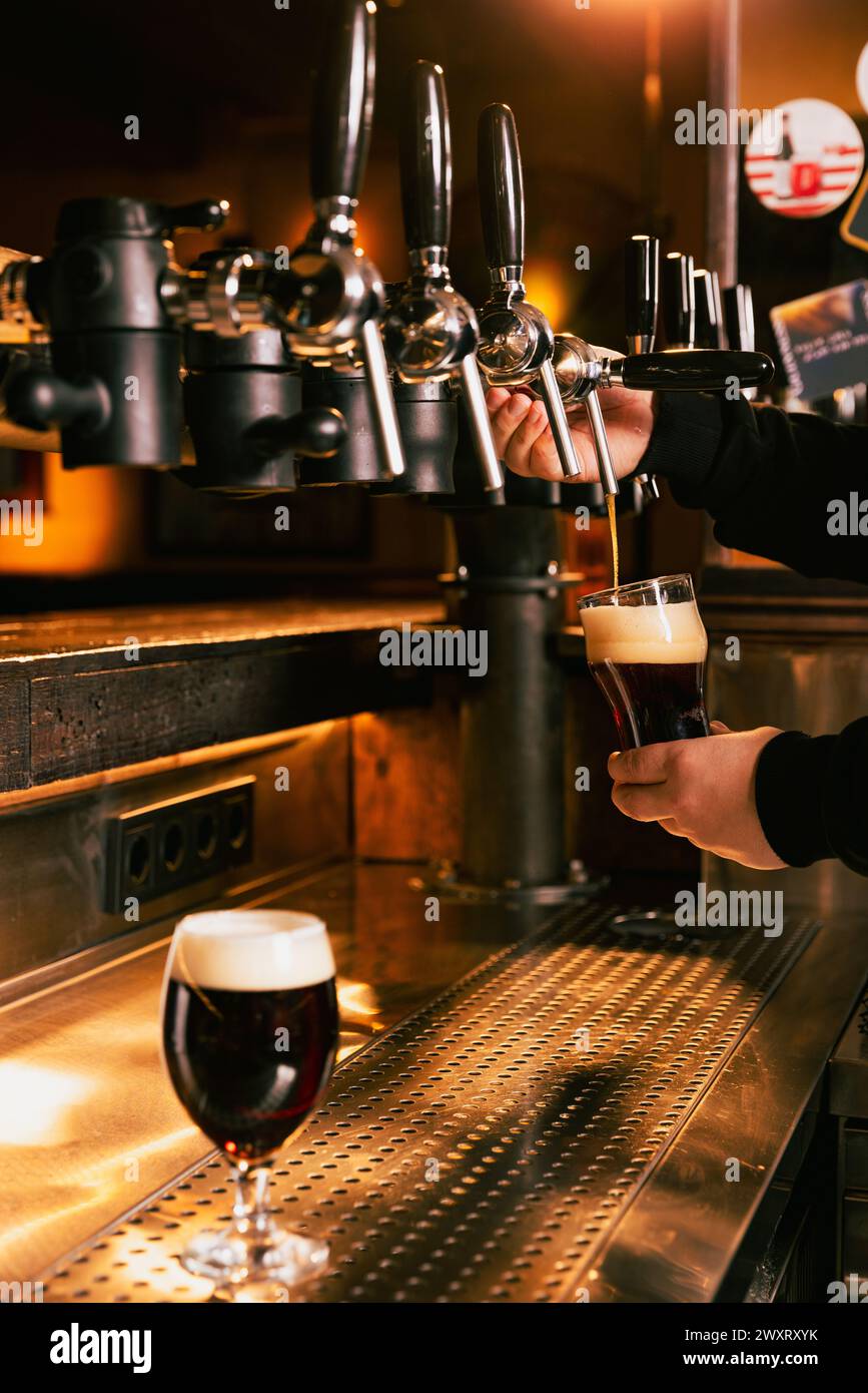 Craft lager beer. Pouring rich, foamy, cold dark beer at bar with array ...