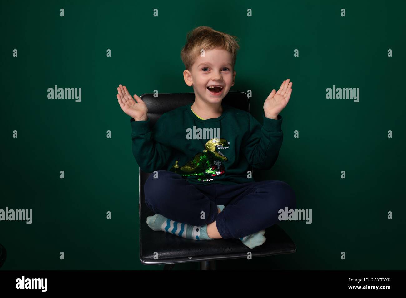 European blond boy smiling cutely sitting on a chair on a green ...