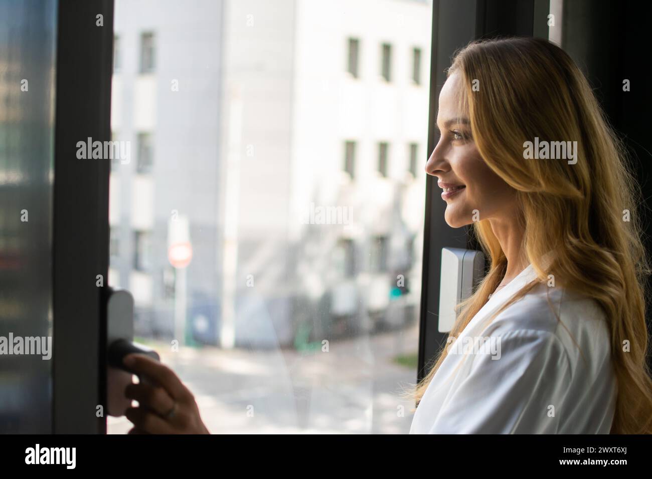 Side view of a pensive young woman looking out a bright window in a ...
