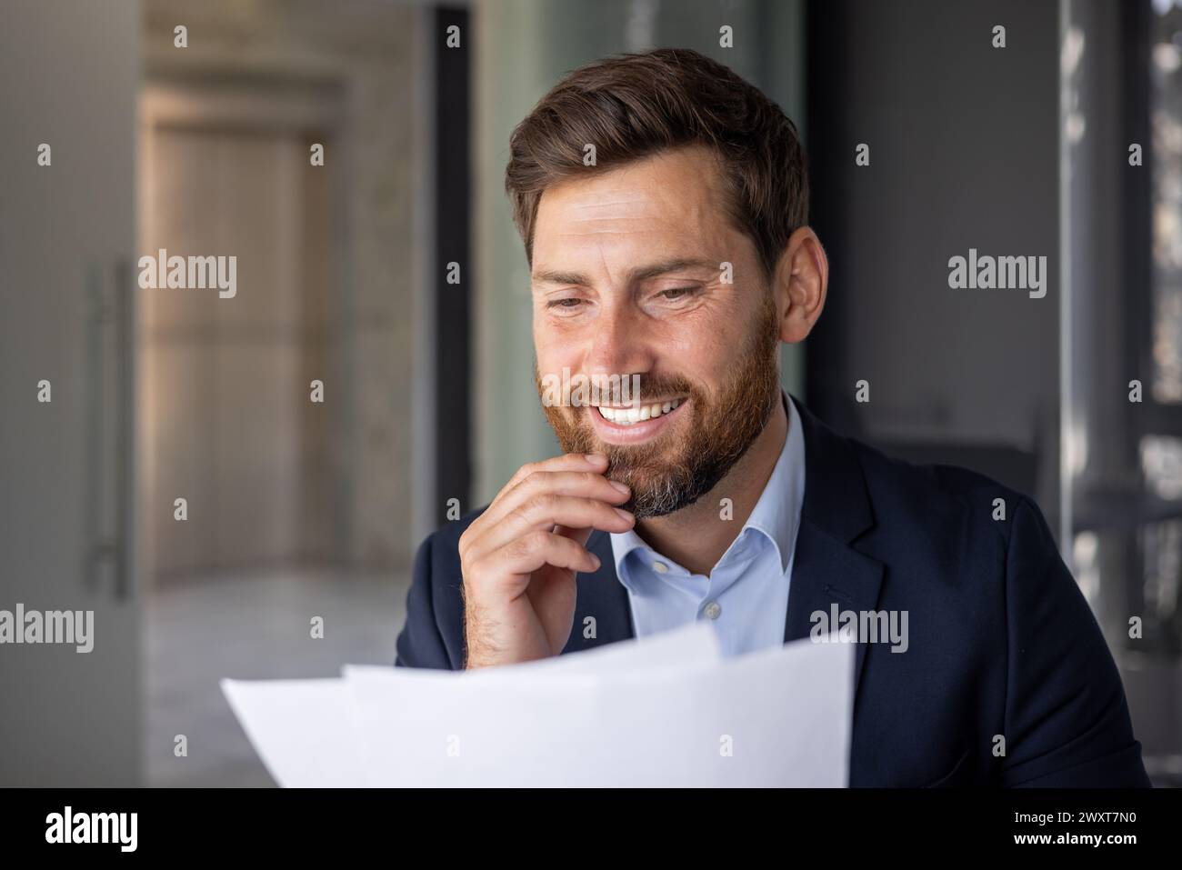 A smiling businessman in a suit examines papers, portraying confidence ...