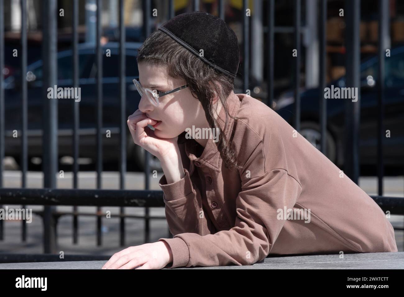 A pensive yeshiva student seems lost in thought during outdoor recess ...