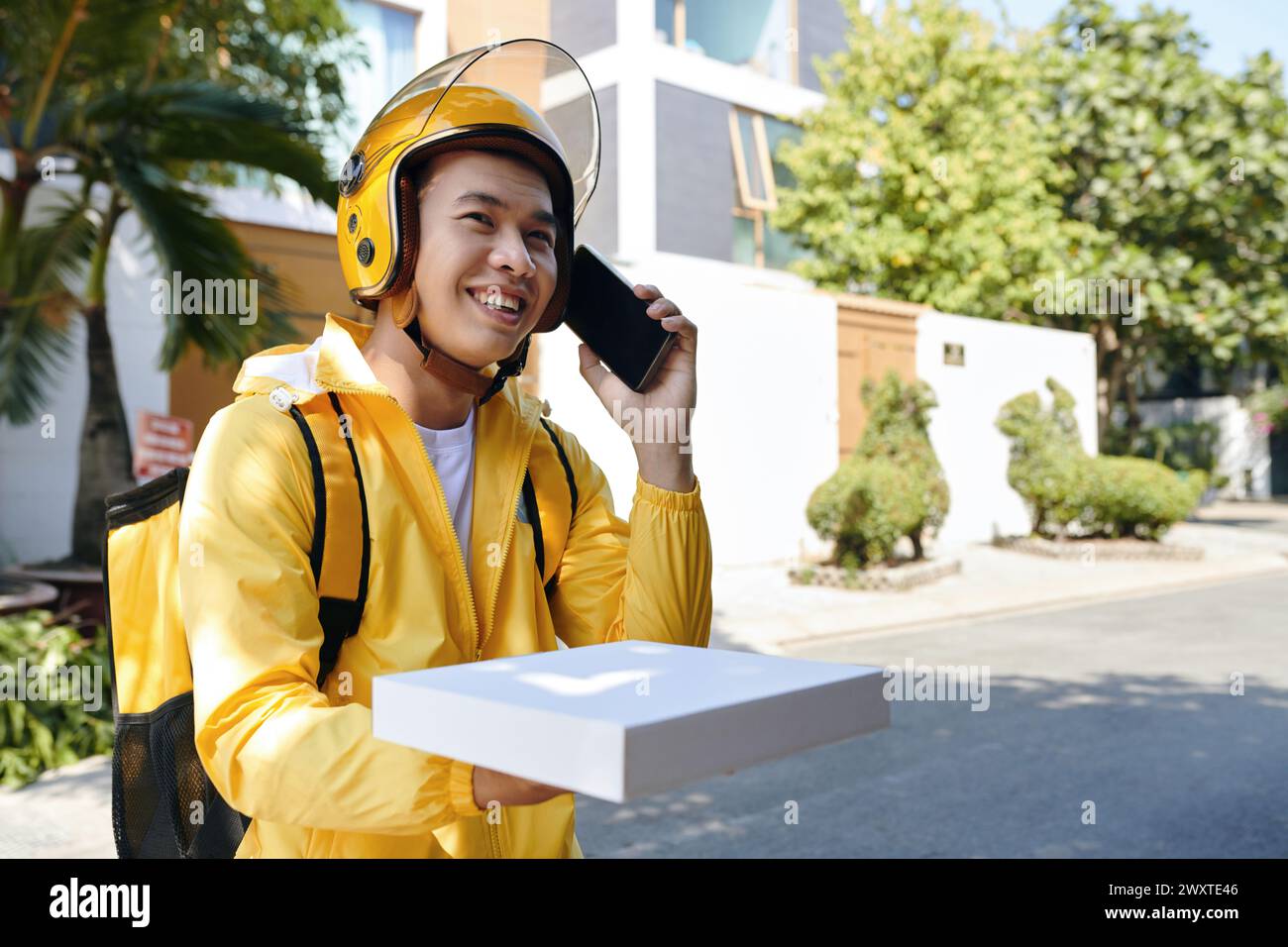 Smiling delivery man with box of pizza standing in font of customer ...