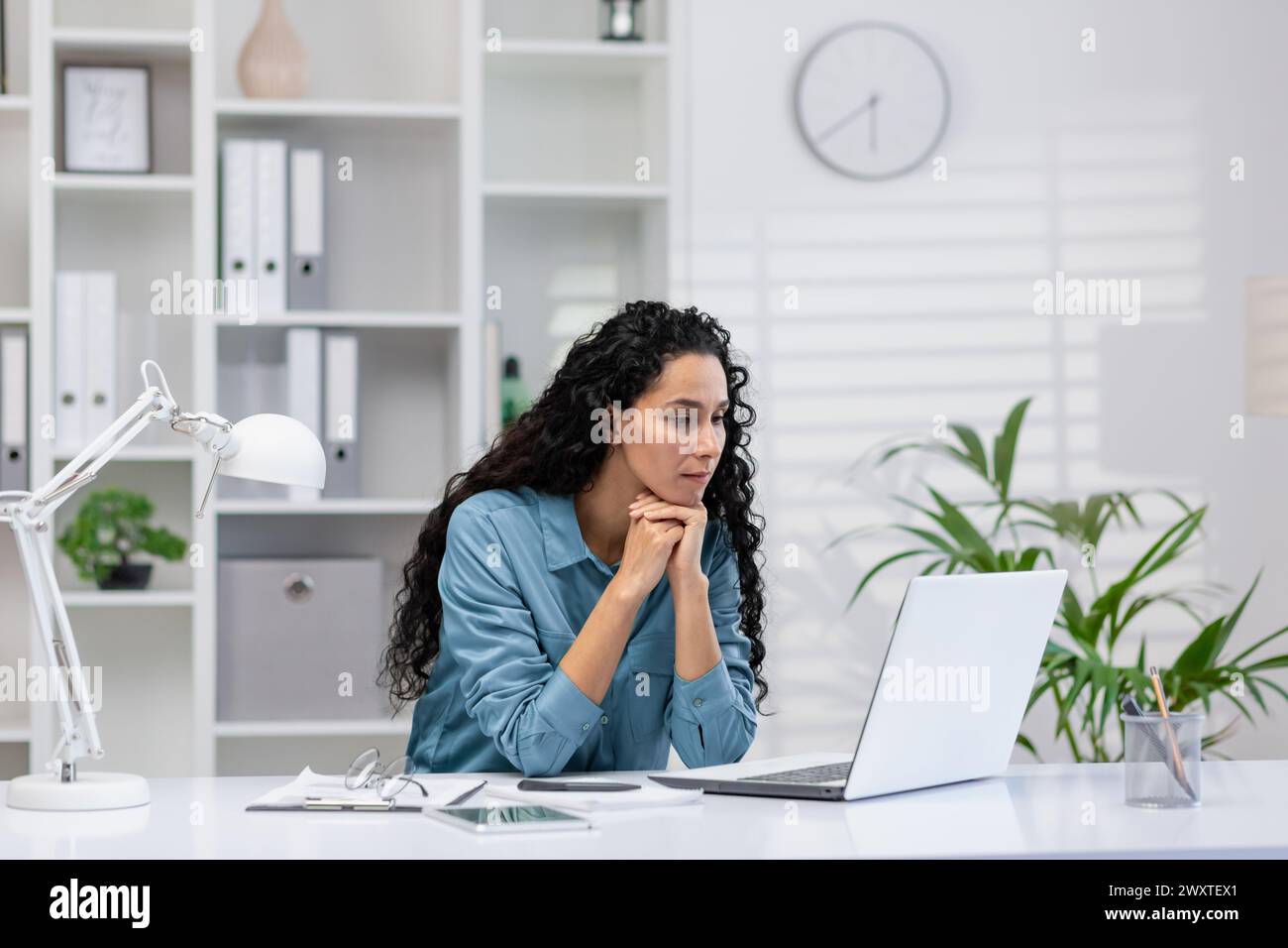 Focused Hispanic woman working on her laptop from a well-organized home ...
