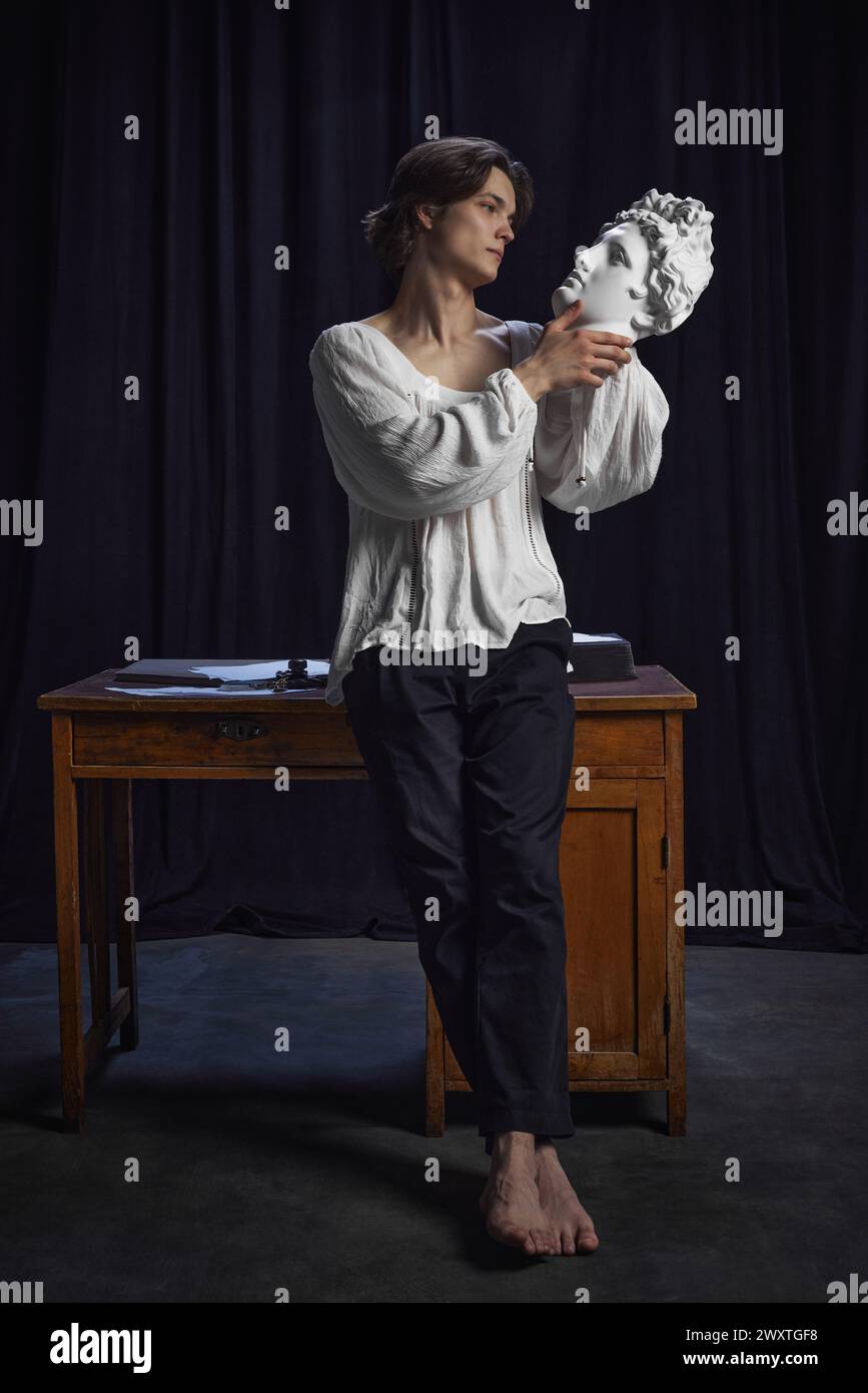Young man, poet in historical costume examining classical sculpture ...