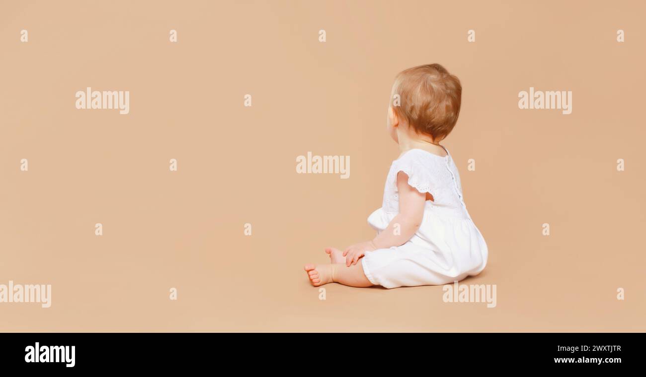 Happy cute baby sitting on the floor on brown studio background, back ...