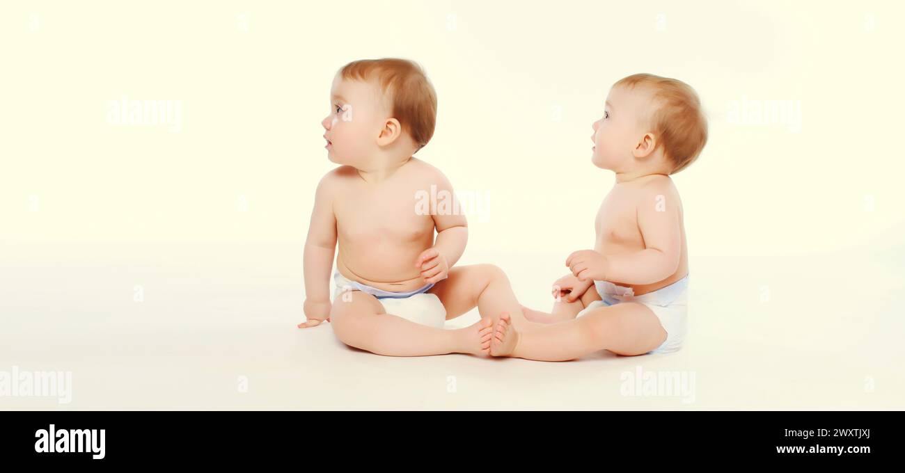Cute two twin babies in diapers sitting on the floor on white studio ...