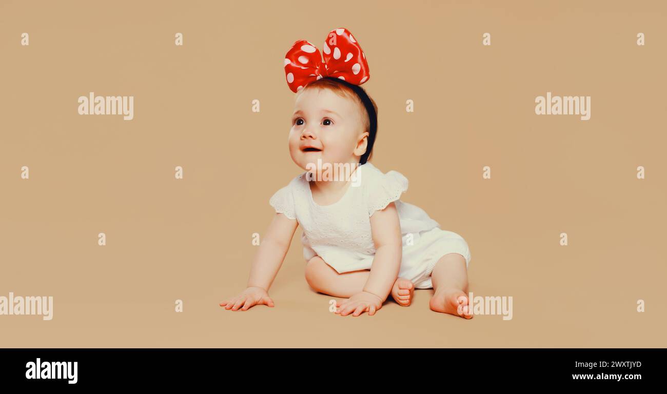 happy cute baby with bow on the head crawling on the floor on brown ...