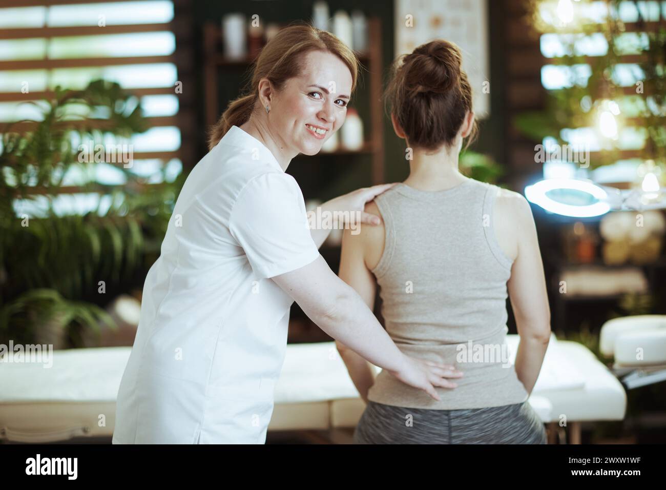 Healthcare time. happy massage therapist in massage cabinet checking clients back condition ...