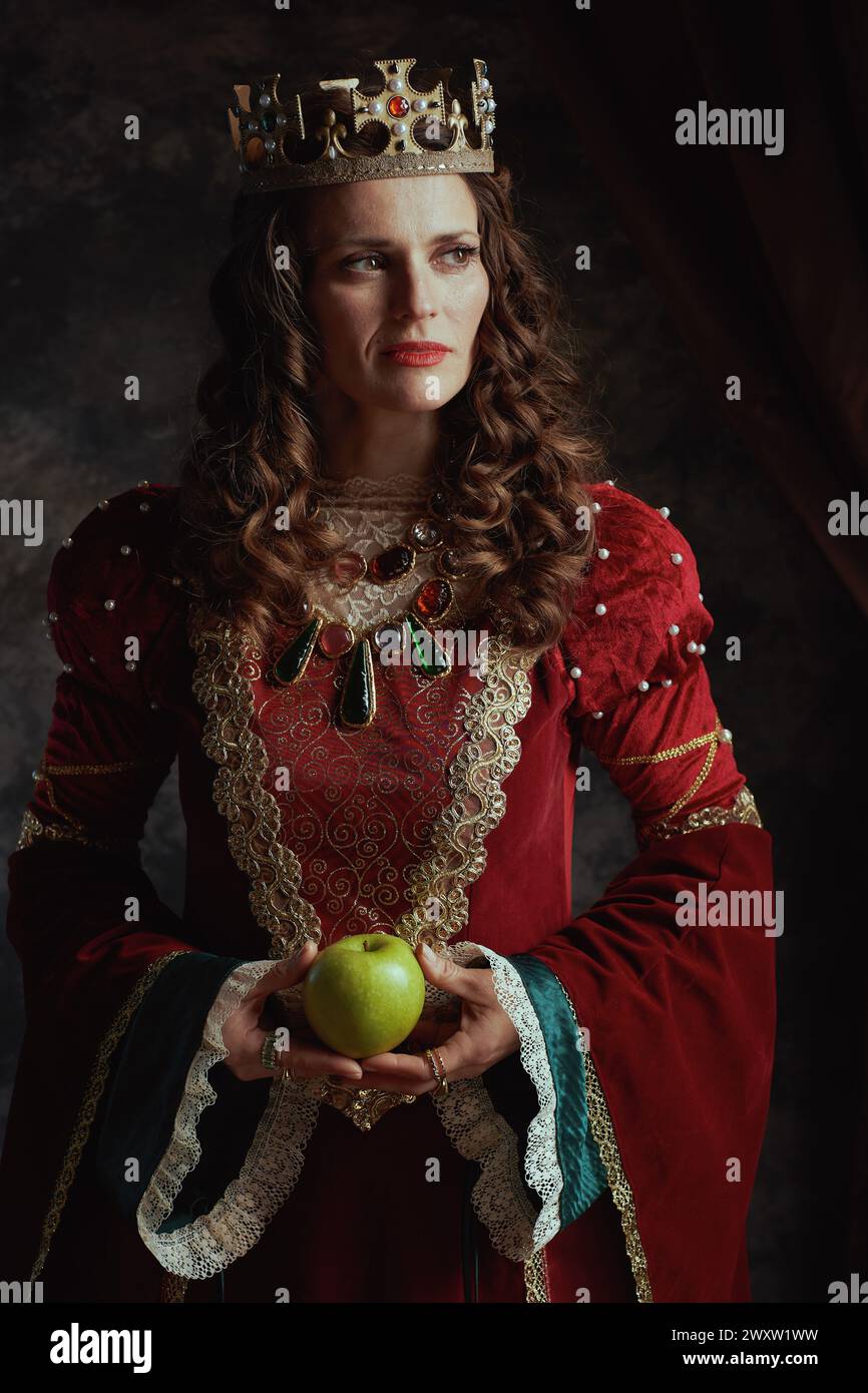 medieval queen in red dress with green apple and crown on dark gray ...