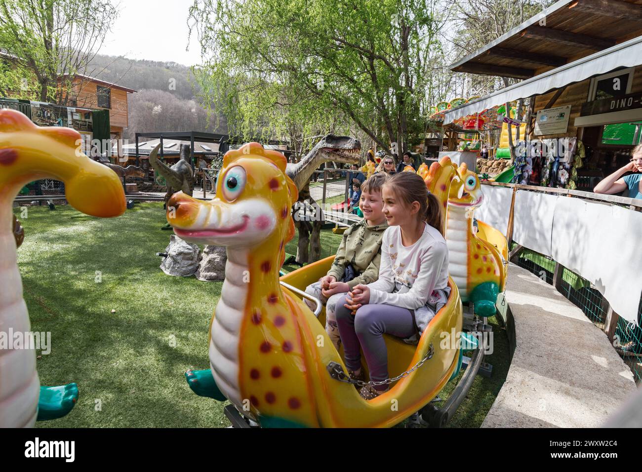 Children on a dinosaur roller coaster outdoor in an amusement park in ...