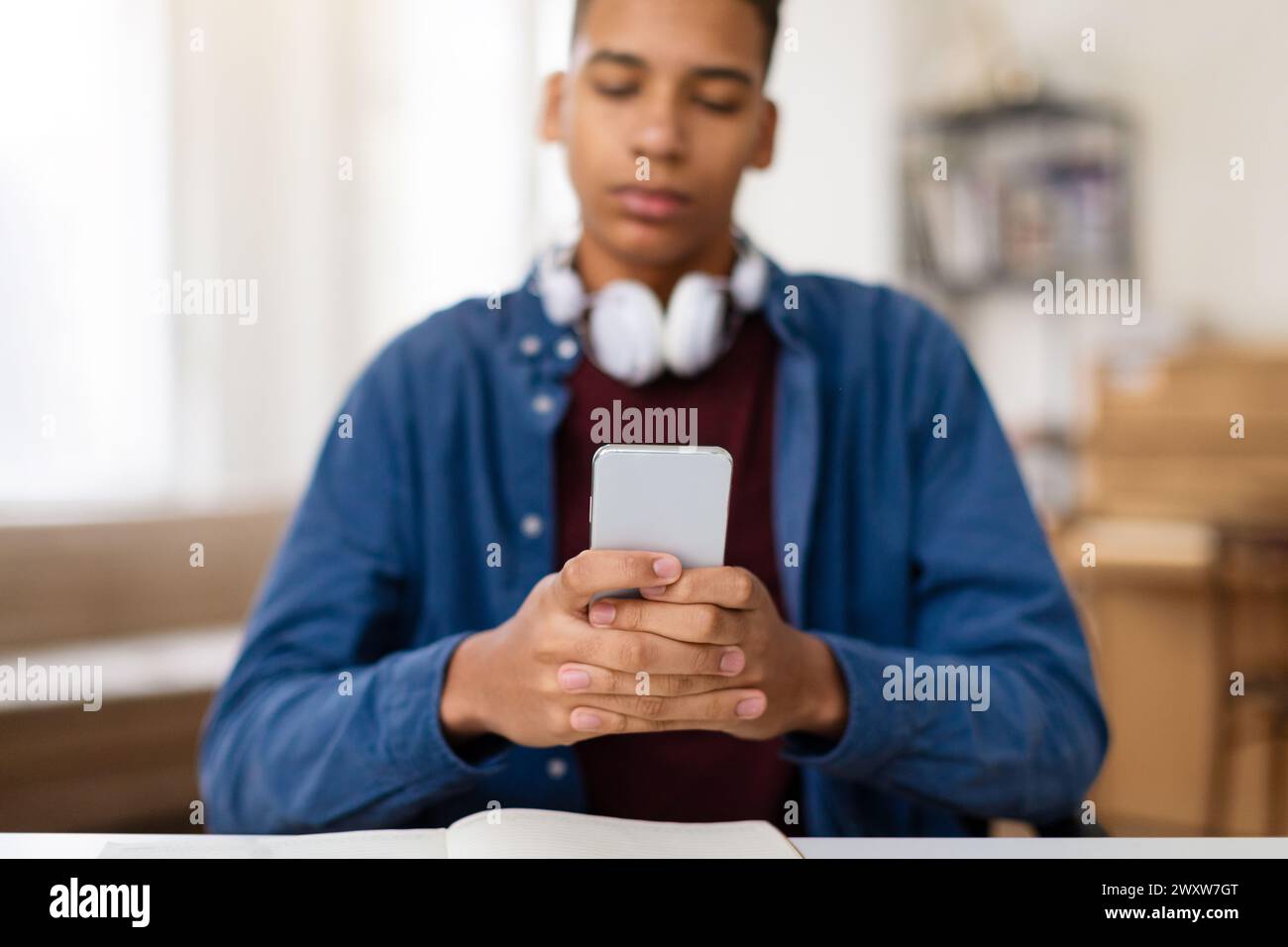 Focused black teen guy using phone with headphones around neck Stock ...