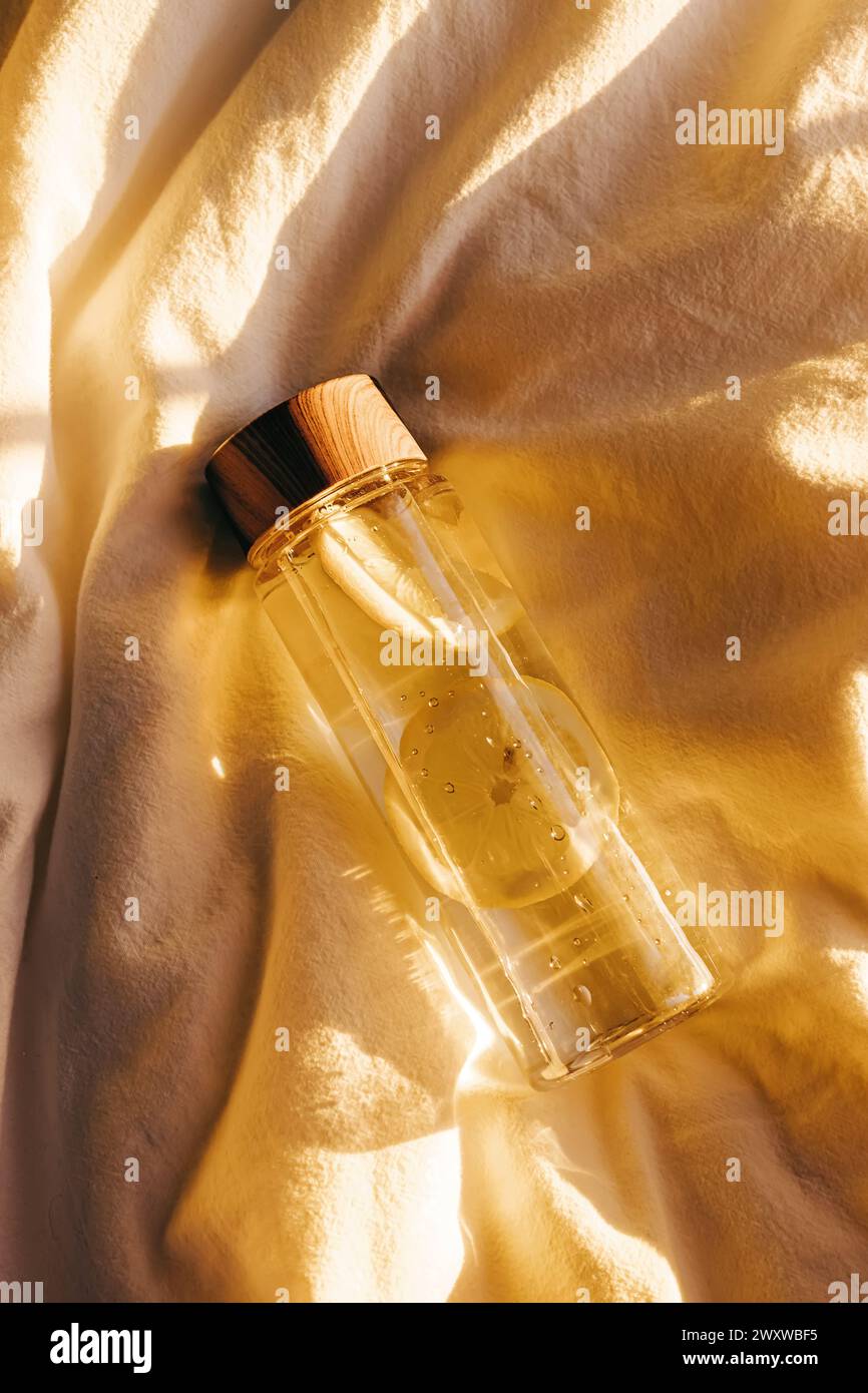 Reusable bottle with lemon infused water in warm natural light on the bed, self-care and ...