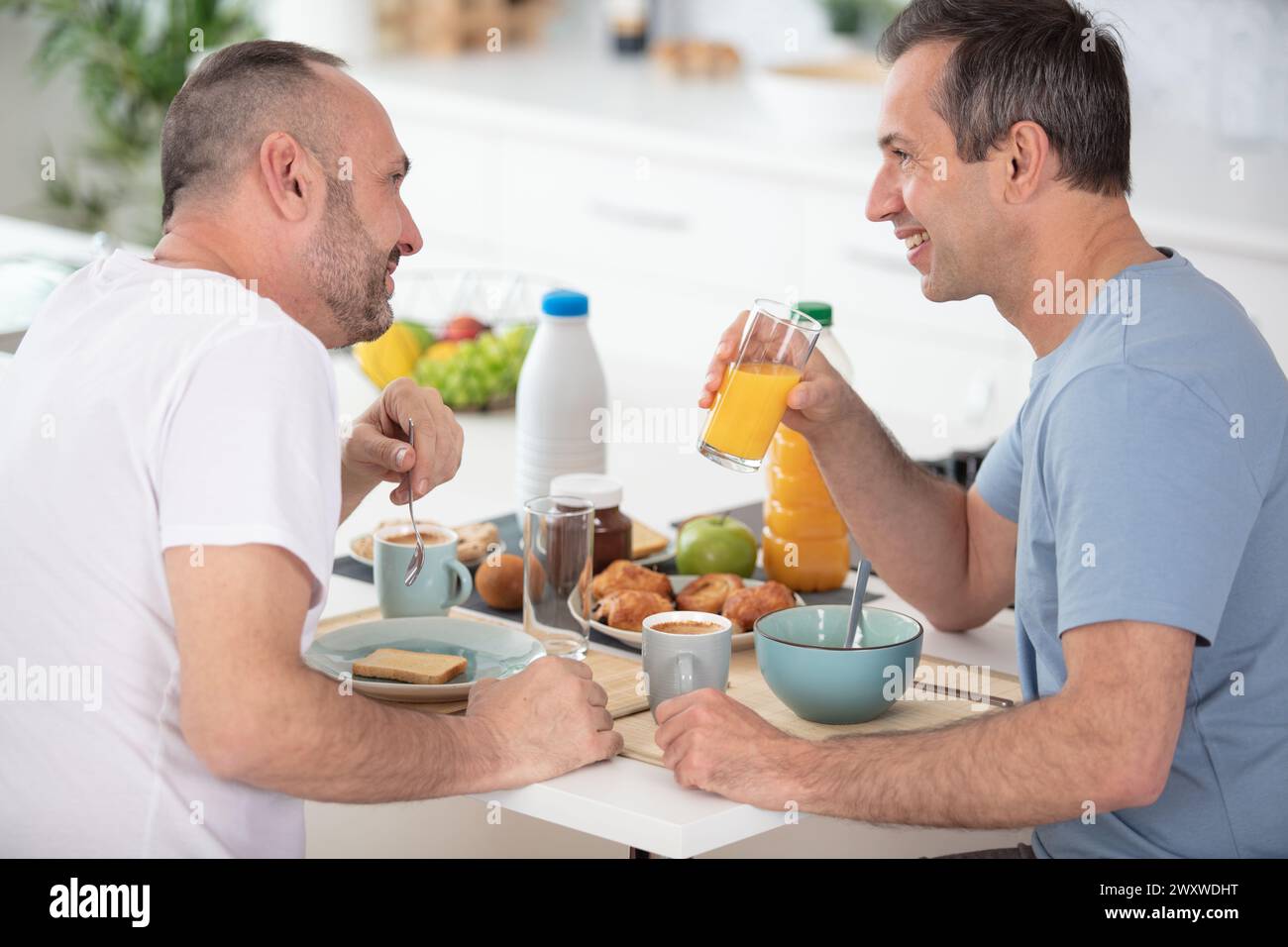 happy male partners eating breakfast and cooking in kitchen Stock Photo ...